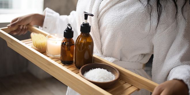 Frau im Bademantel hält ein Badewannentablett in der Hand.