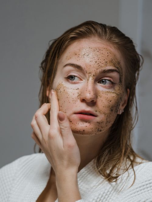 blonde Frau die sich gerade ein Peeling im Gesicht aufträgt.