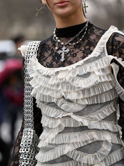 Street Style Look von der New York Fashion Week, wo ein Gast ein Spitzenkleid und Spitzenbluse mit Silberschmuck kombiniert.