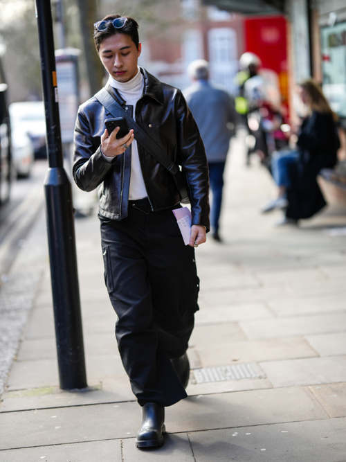 Street Style Foto von der London Fashion Week, wo ein Gast eine schwarze Lederjacke mit weißem Rollkragenpullover und schwarzer Hose trägt.
