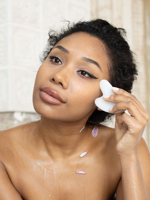 Frau mit einem schwarzen Lidstrich fährt sich mit einem Gua Sha Stein über die Wange.