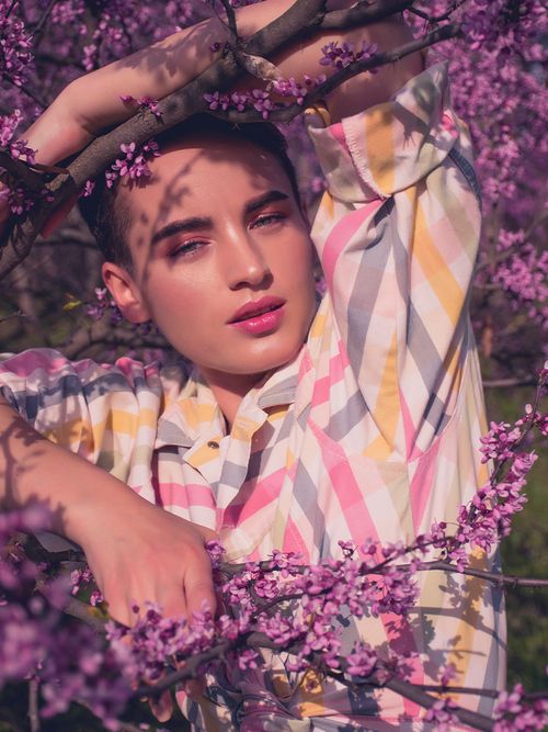 Frau mit raspelkurzen Haaren und einer gestreiften Bluse die in einem blühenden Baum lehnt.