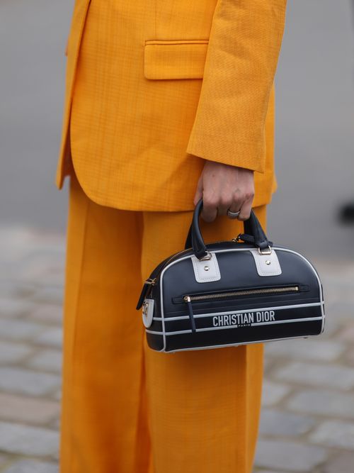 Street Style Look von der Paris Fashion Week, wo ein Gast einen orangen Hosenanzug trägt und eine Bowling-Tasche von Christian Dior in der Hand hält.