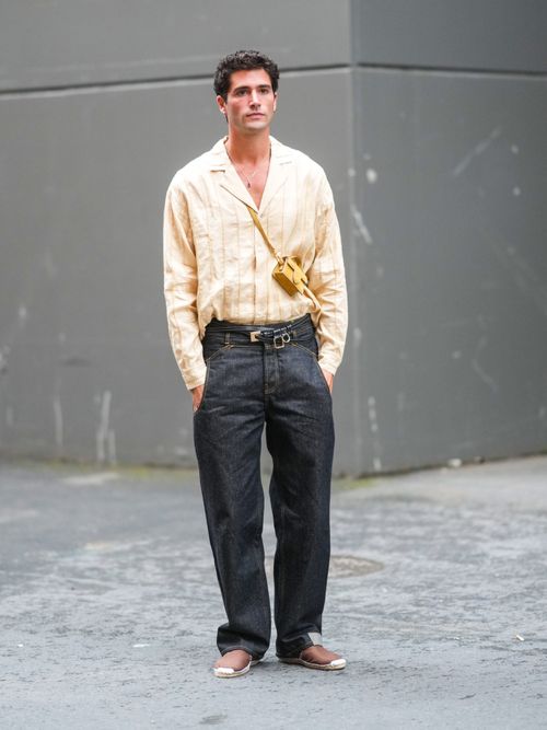 Marc Forne trägt ein gelb-gestreiftes Bowlinghemd mit Jeans, Gürtel und Umhängetasche auf der Jacquemus Show in Frankreich.
