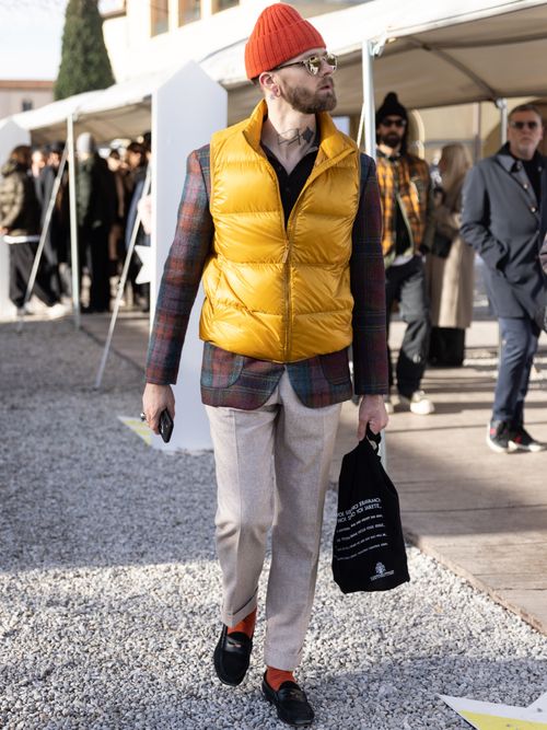 Street Style Look von einem Mann der ein Karo-Sakko mit einem gelben Gilet und grauer Hose in Florenz trägt.