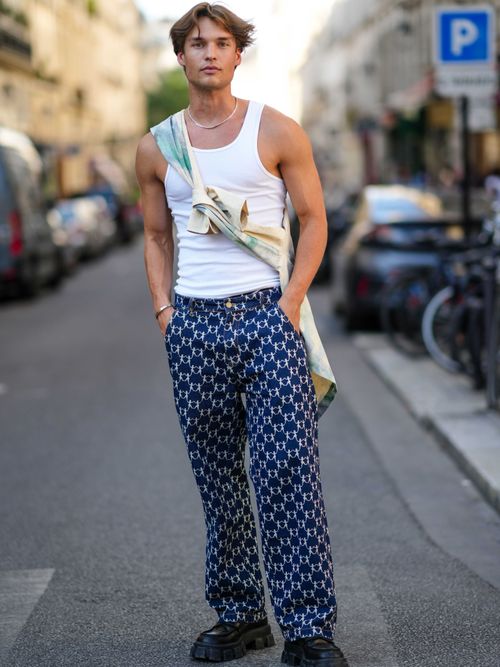 Street Style von der Paris Fashion Week, wo ein Mann ein gemusterte Jeans mit Tank Top und buntem Pullover trägt.