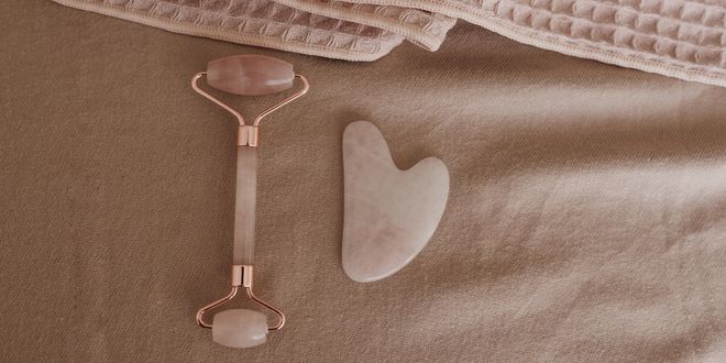 Ein Gua Sha Stein und ein rose Beauty Roller liegen auf einem rosa Handtuch.