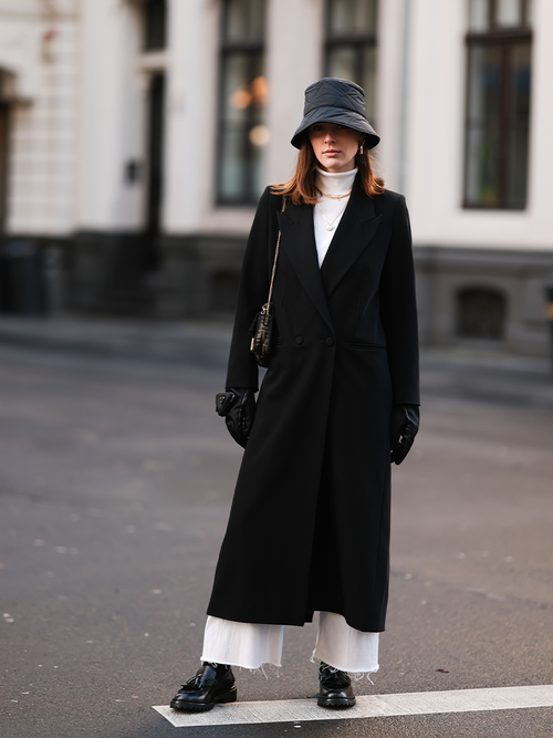 Streetstyle mit einem schwarzen Wollmantel, einem weißen Rollkragenpullover und einem schwazen Bucket Hat.