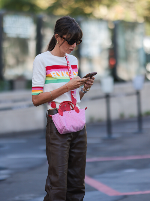 Street Style Look von der Paris Fashion Week, wo ein Gast eine buntes T-Shirt, eine Lederhose, mit einer Crossbody Longchamp Tasche.