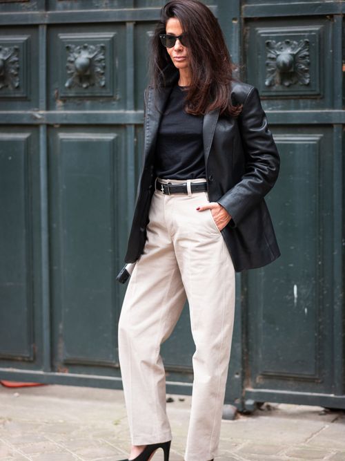 Street Style Look von der Paris Fashion Week wo ein Gast einen Lederblazer mit schwarzem Top, Gürtel und weißer Hose und High Heels trägt.