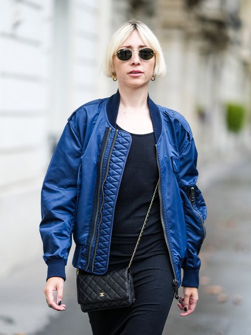Streetstyle von einer Frau mit einem wasserstoffblonden kurzen Bob und einer blauen Bomberjacke.