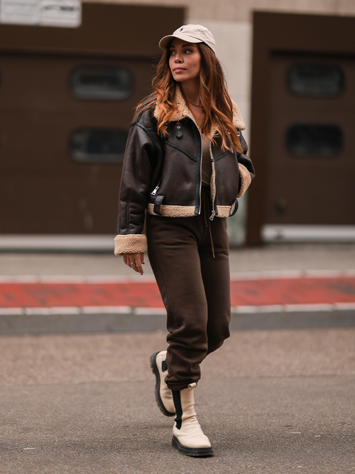 Streetstye mit einer braunen Hose einer Shearling Jacke und einem weißen Cap.