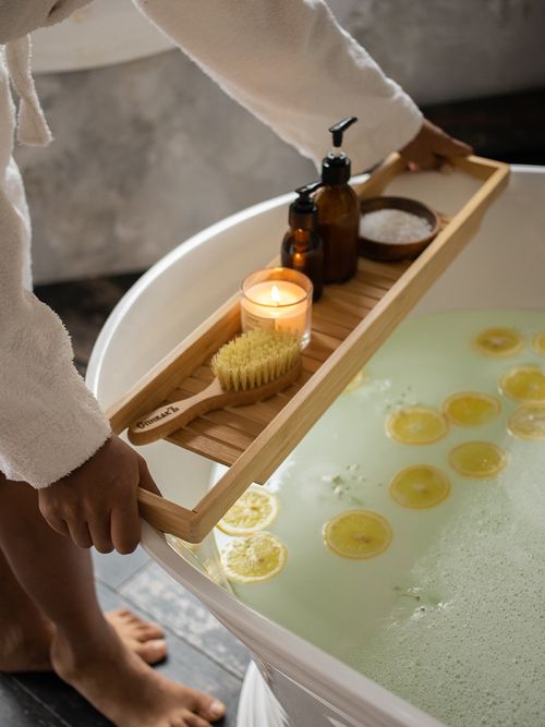 Frau im Bademantel stellt gerade eine Badewannentablett auf einer weißen Badewanne ab.