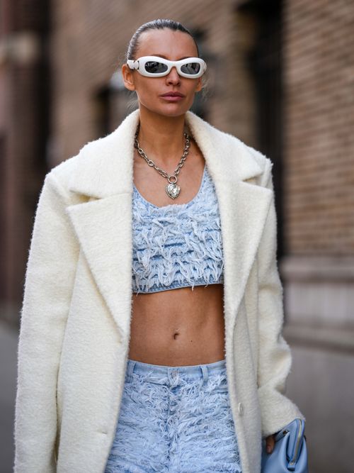 Street Style Look von der New York Fashion Week, wo ein Gast eine weiße Sonnenbrille, dazu einen weißen Mantel und ein hellblaues Ensemble trägt.