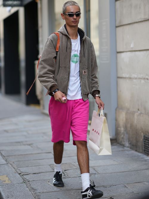 Street Style Look von der Paris Fashion Week, wo ein Mann einen grauen Hoodie von Carhartt WP, weißes T-Shirt, pinke Shorts, weiße Socken und Onitsuka Tiger Sneaker trägt.