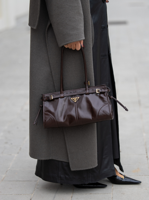 Gili Biegun trägt eine braune Prada Tasche zu einem grauen Mantel und schwarzem Rock in Barcelona.