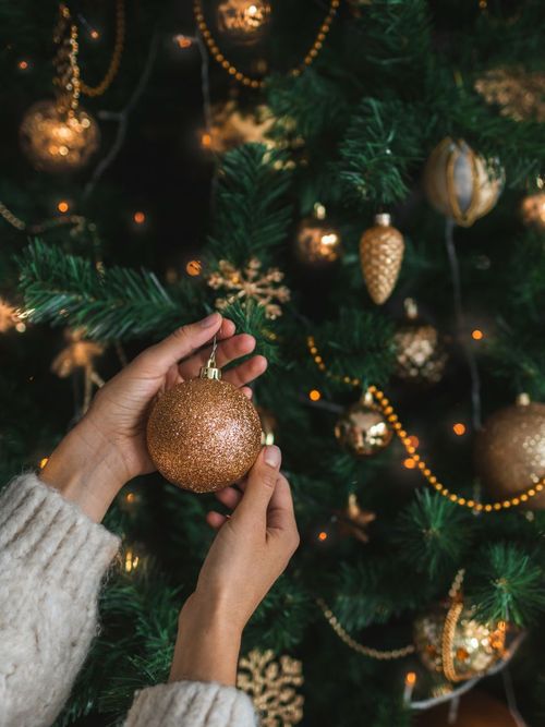 Frauenhand die gerade dabei ist den Christbaum zu schmücken mit goldenen Baumschmuck