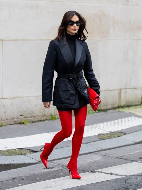 Street Style Look von der Paris Fashion Week, wo ein Gast einen schwarzen Boyfriend-Blazer mit schwarzen Rollkragen, roten Strümpfen und roten Pumps trägt.