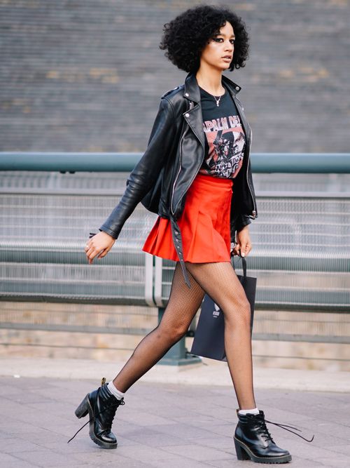 Ein Model trägt eine Lederjacke, roten Rock und feine Netzstrümpfe auf der London Fashion Week