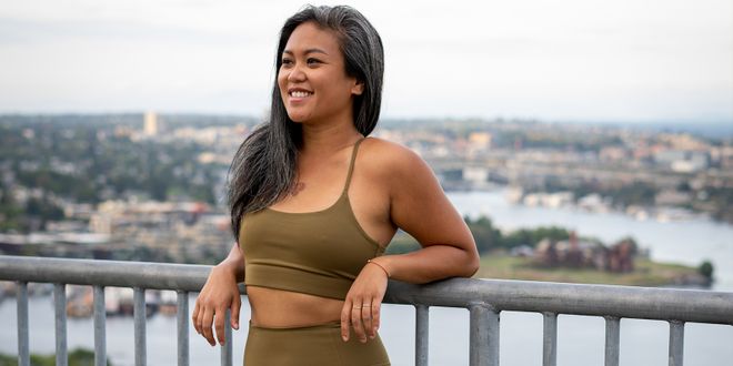 Frau in Work-out-Kleidung, die sich lachend an einen Zaun lehnt.