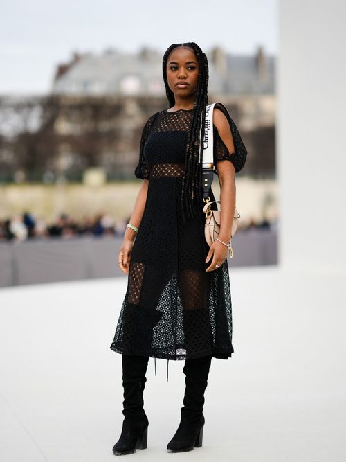Street Style Look von der Paris Fashion Week, wo ein Gast ein schwarzes transparentes Kleid mit Radlerhose darunter und Stiefel trägt.