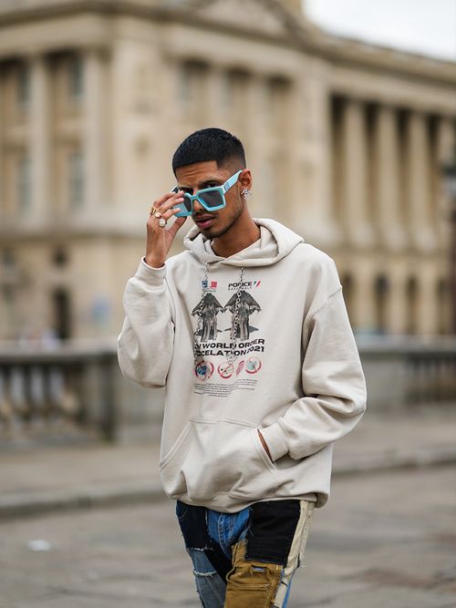 Streetstyle mit einem Mann in einem weißen Sweatshirt und einer Sonnenbrille mit blauen Gläsern.