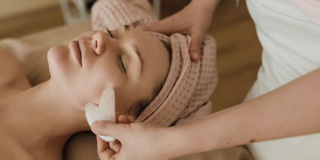 Frau mit rosa Handtuch-Turban wird mit einem rosa Gua Sha Stein behandelt.