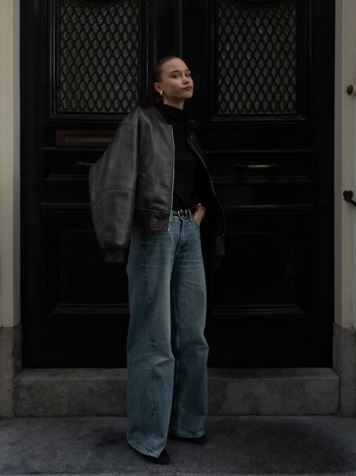 Street Style Look von einer Frau, die ein schwarzes T-Shirt, graue Bomberjacke und weite Jeans trägt.