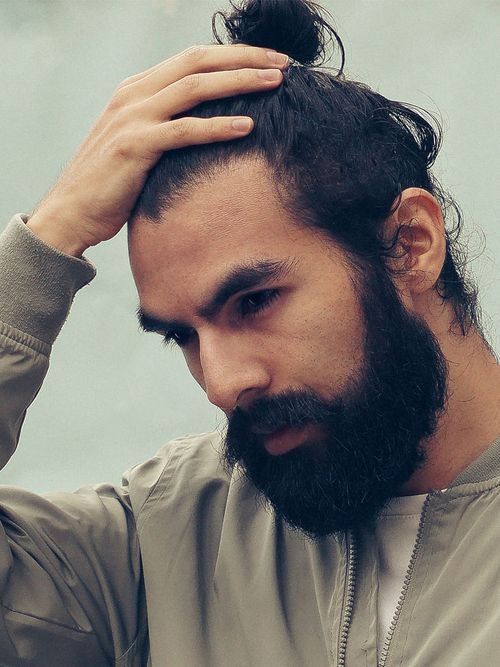 Mann mit Vollbart und einem Man Bun greift sich auf die Stirn.