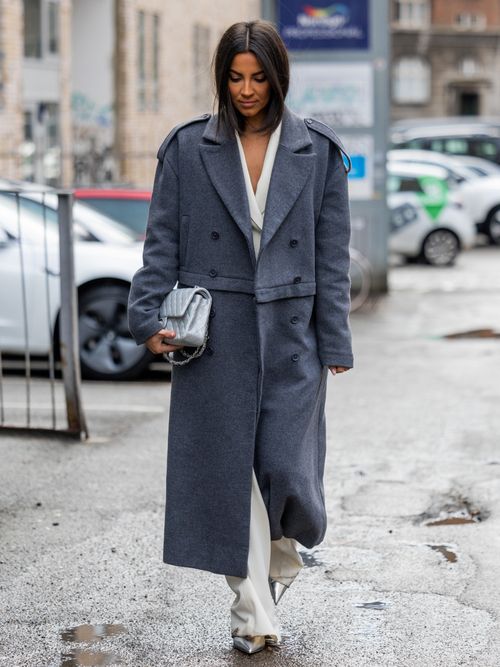 Stephanie Abu-Sbeih trägt einen grauen Mantel, weißes Oberteil und weiße Hose, mit silbernen High Heels und einer Chanel Tasche auf der Copenhagen Fashion Week.