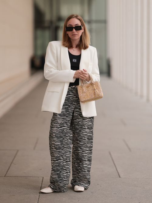 Sonia Lyson trägt einen weißen Blazer, schwarzes Top mit Logo, Zebra-Hose und eine Glitzertasche in Berlin.