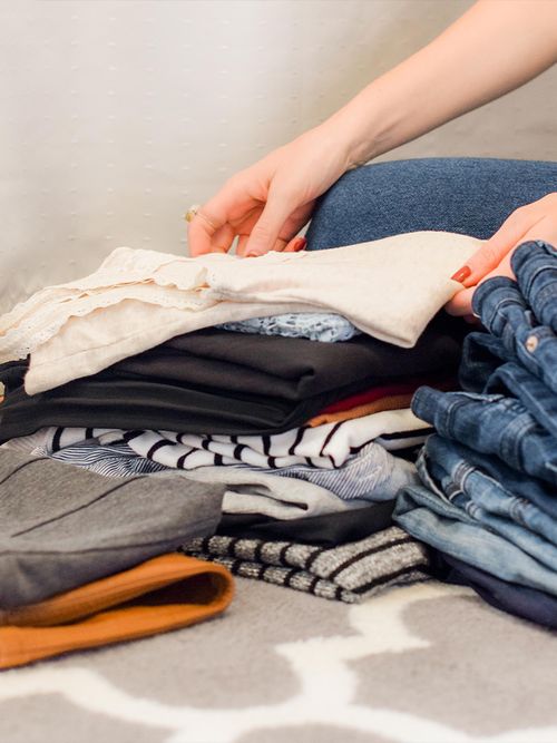 Frauenhände, die 3 Stapel an Kleidung, vorwiegend Jeans zusammenfalten.