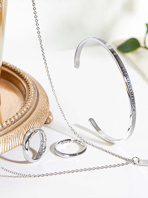 Silberne Schmuckstücke mit Gravur auf einem weißen Hintergrund.