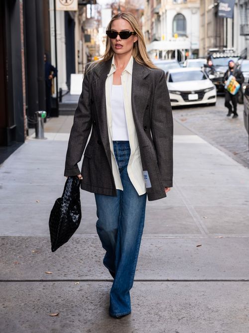 Margot Robbie trägt einen oversized Blazer, weiße Bluse und dunkle Jeans in New York City.
