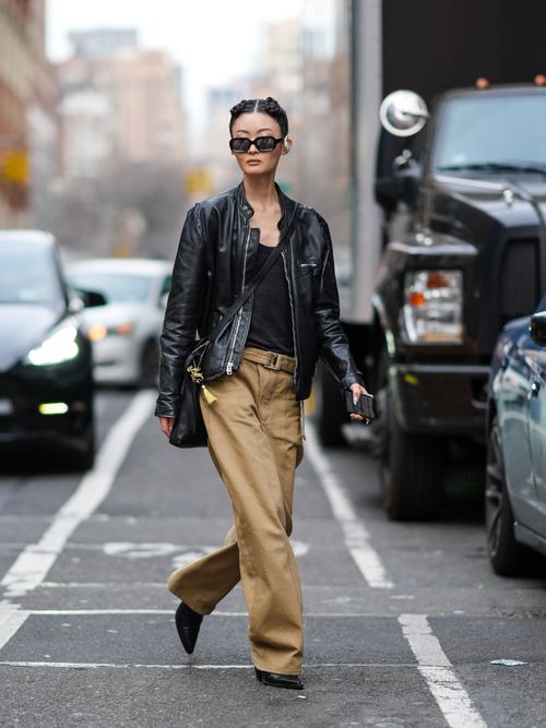 Street Style Look von einer Frau auf der New York Fashion Week, die eine Lederjacke mit schwarzen T-Shirt, beiger Denim und spitze Schuhe trägt.