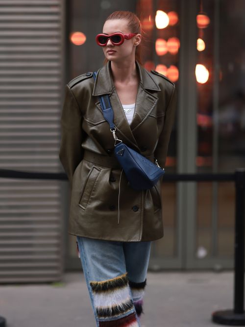 Street Style Look von der Paris Fashion Week, wo ein Gast einen Lederblazer mit Gürtel, eine Denim, eine Sonnenbrille und Crossbody Tasche von Dior trägt.